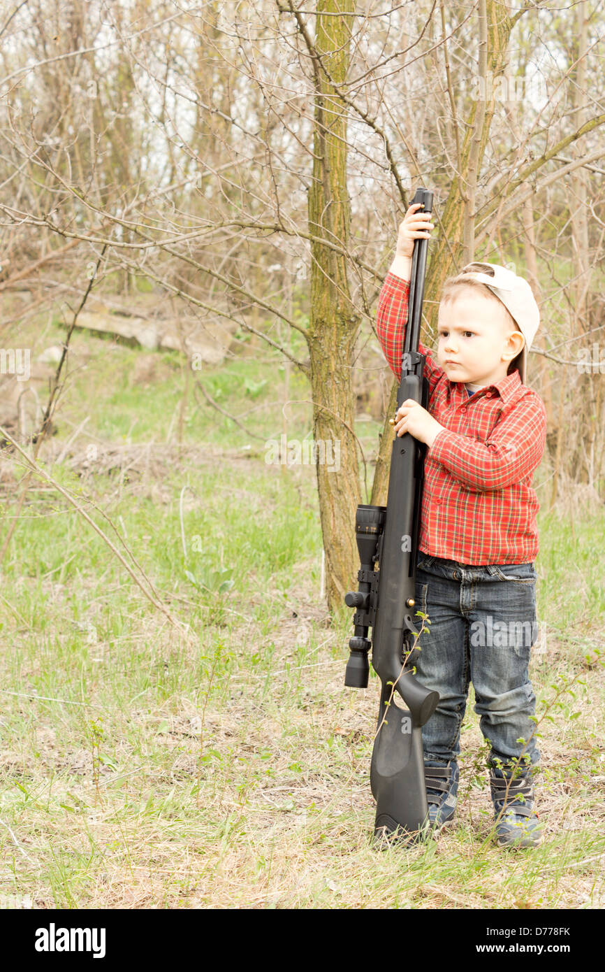 Small boy standing and holding up a large rifle with a scope attached ...