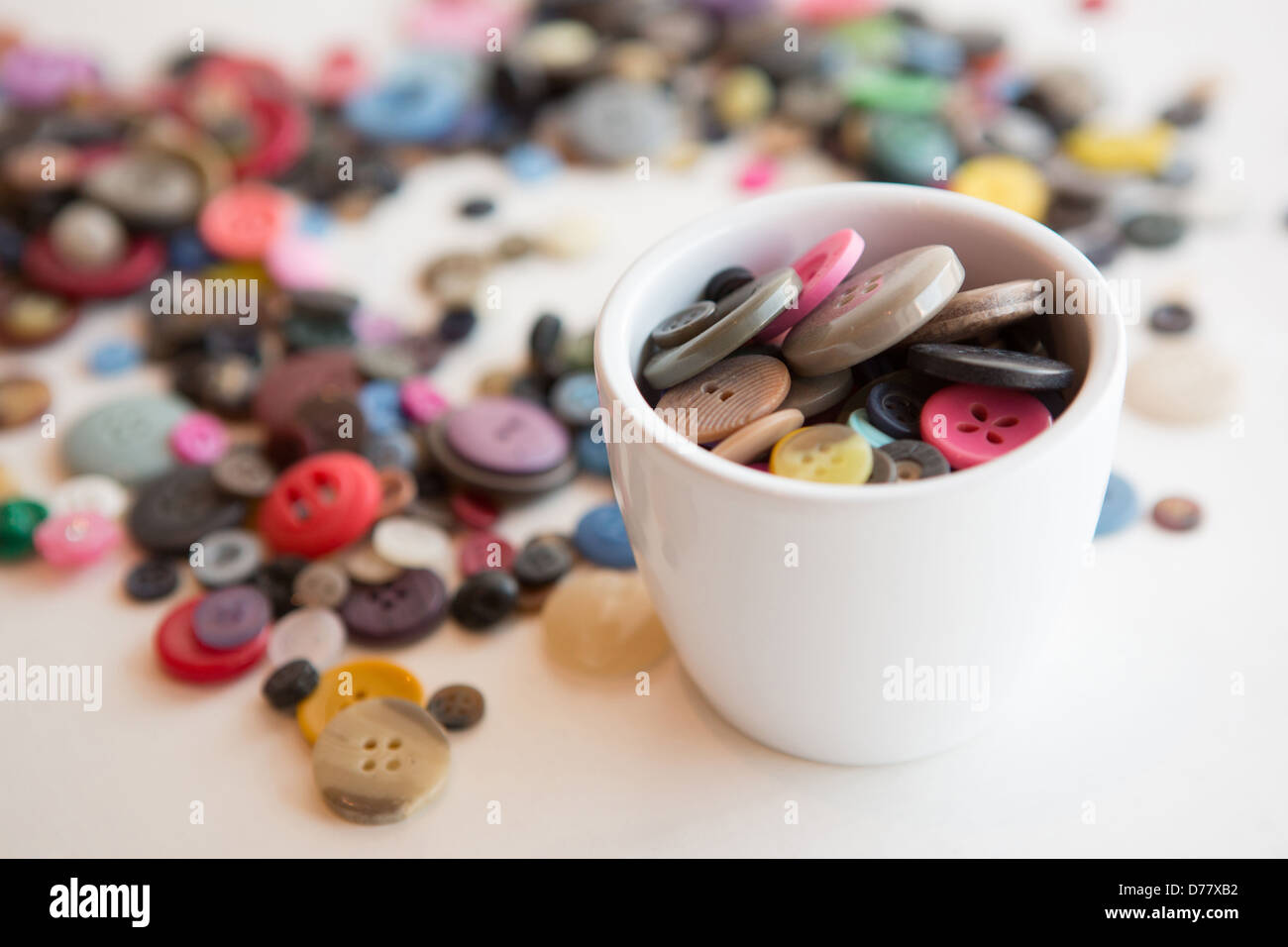 A small white bowl filled with buttons, surrounded by a selection of ...