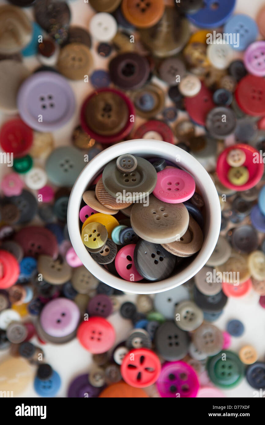 A small white bowl filled with buttons, surrounded by a selection of ...