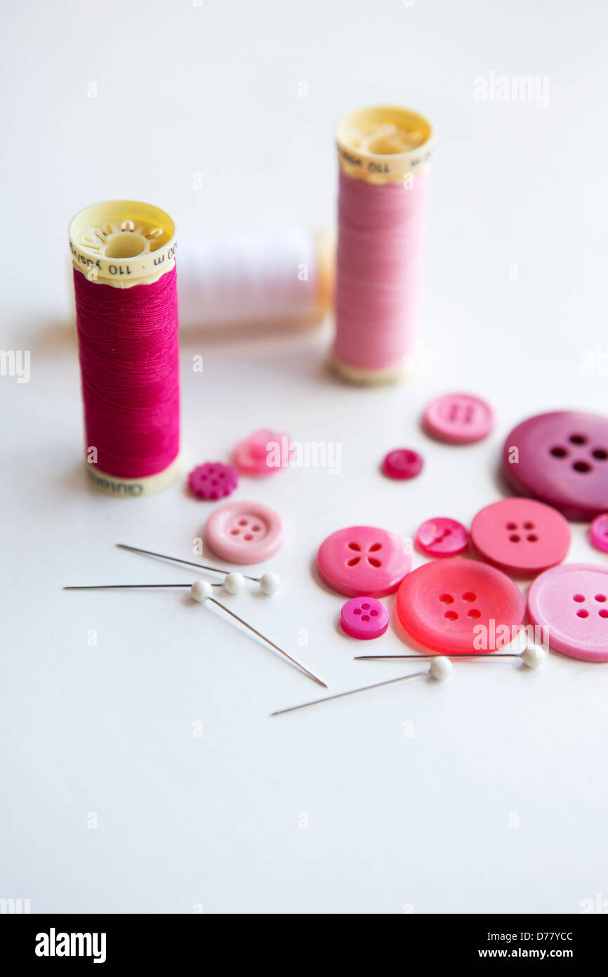A sewing kit of thread, pins and buttons scattered against a light grey ...