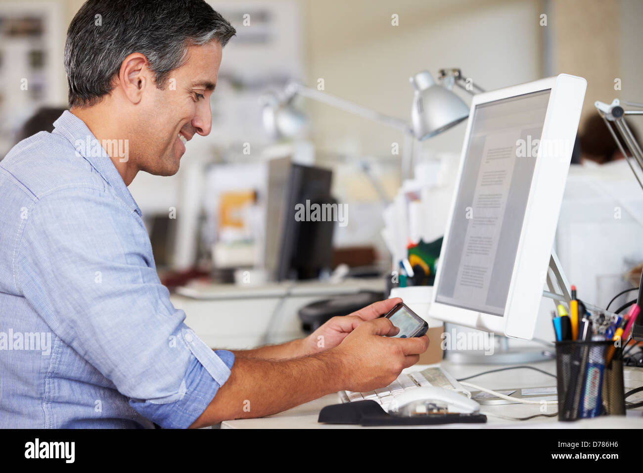 Man Using Mobile Phone At Desk In Busy Creative Office Stock Photo - Alamy