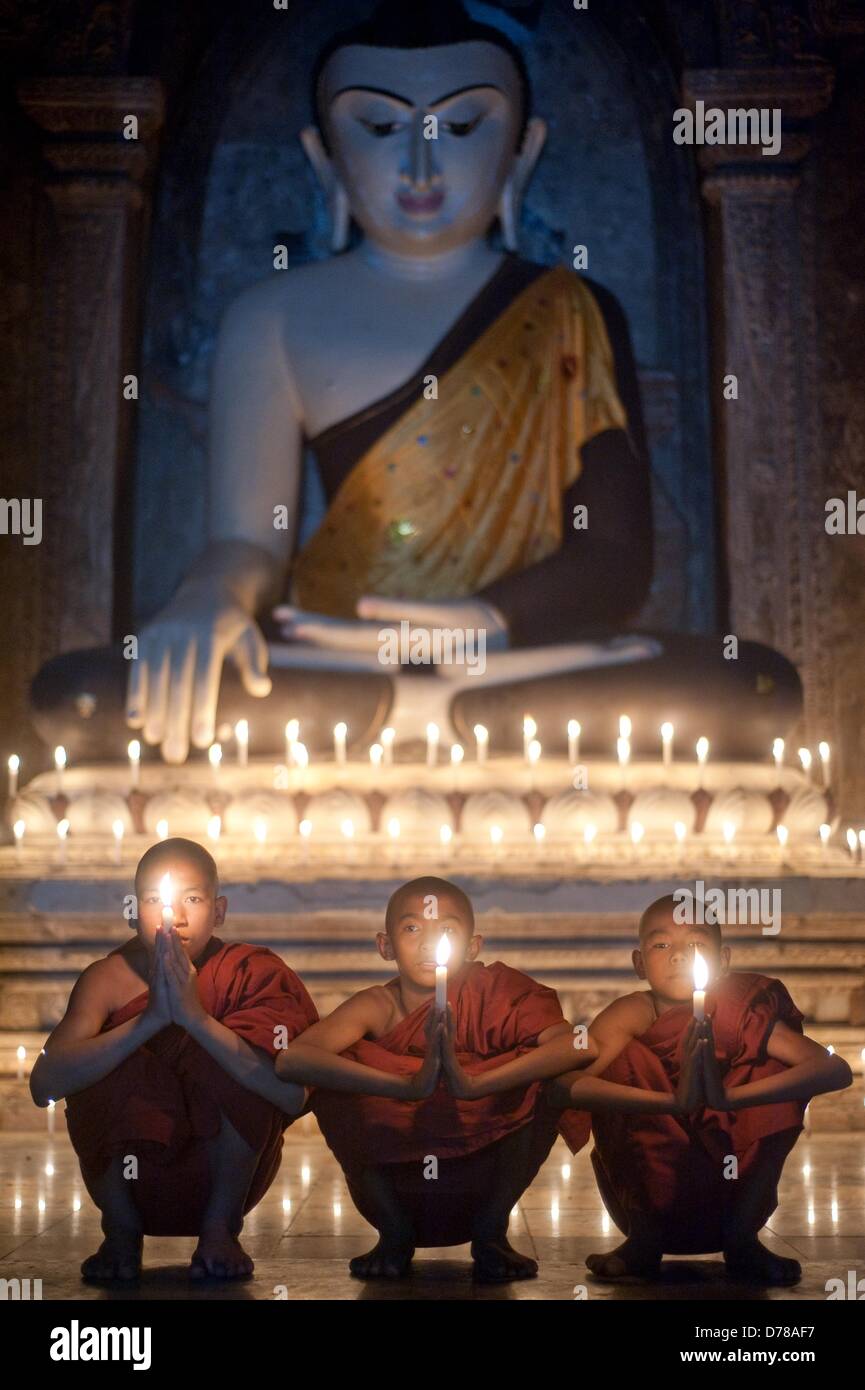 Three young Buddhist monks are squatting with a candle in front of a ...