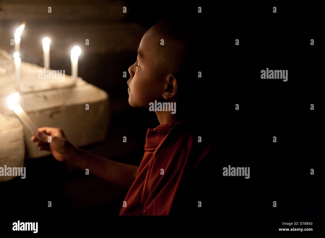 A young Buddhist monk is holding a candle in a temple in Bagan, Myanmar ...