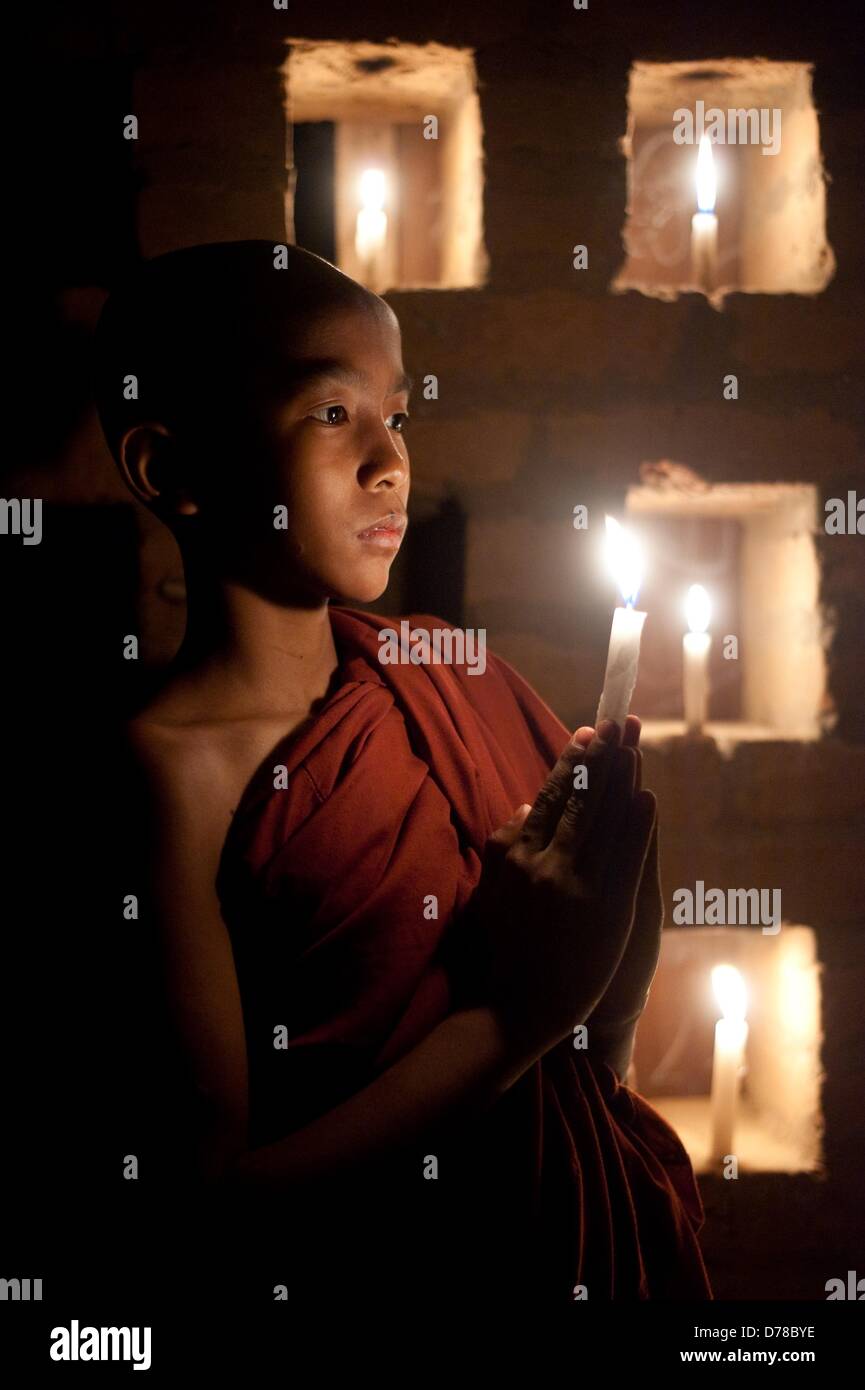 A young Buddhist monk is standing with a candle in a temple in Bagan ...