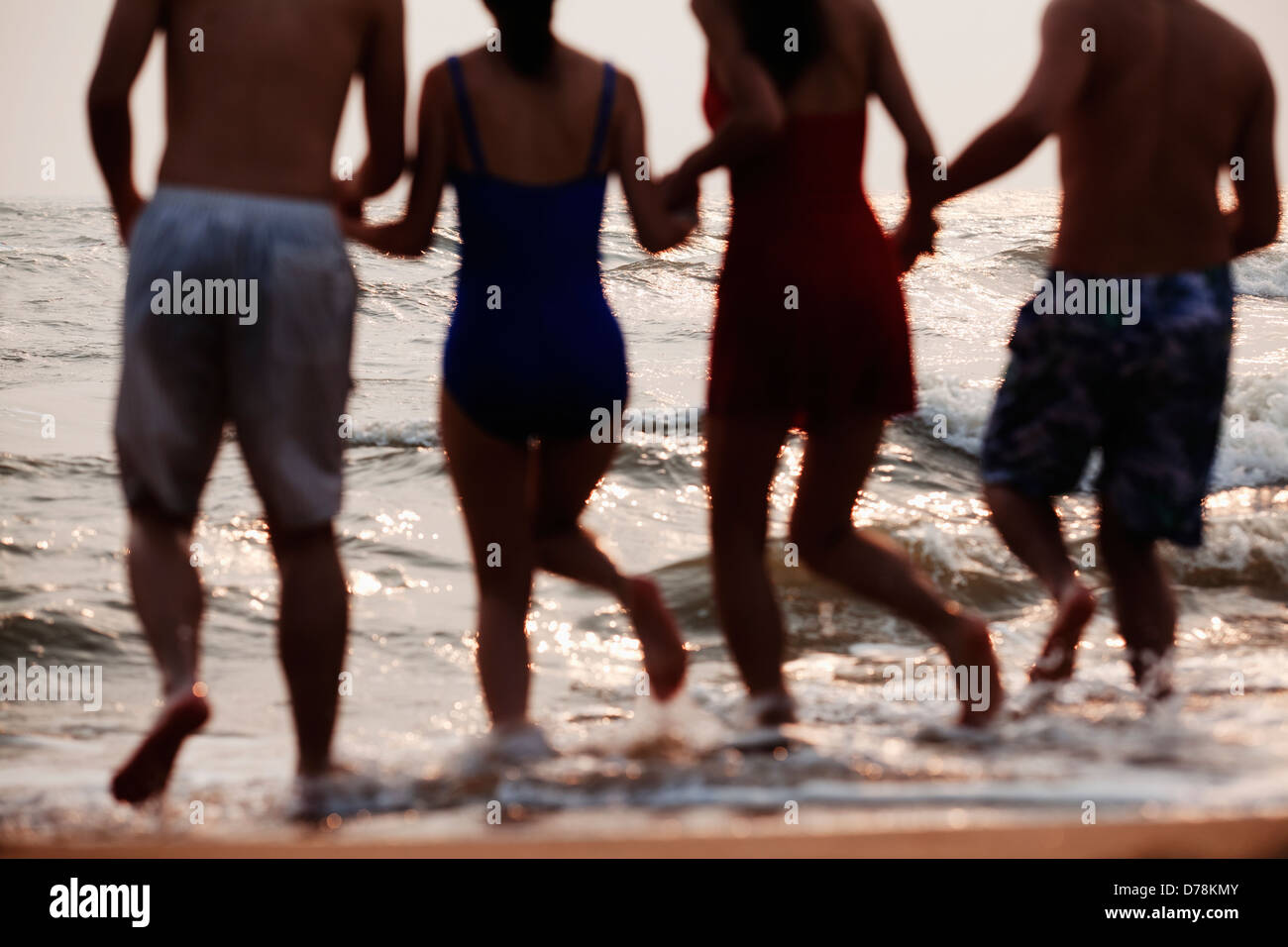 Four friends running into the water on a sandy beach, Silhouette Stock ...
