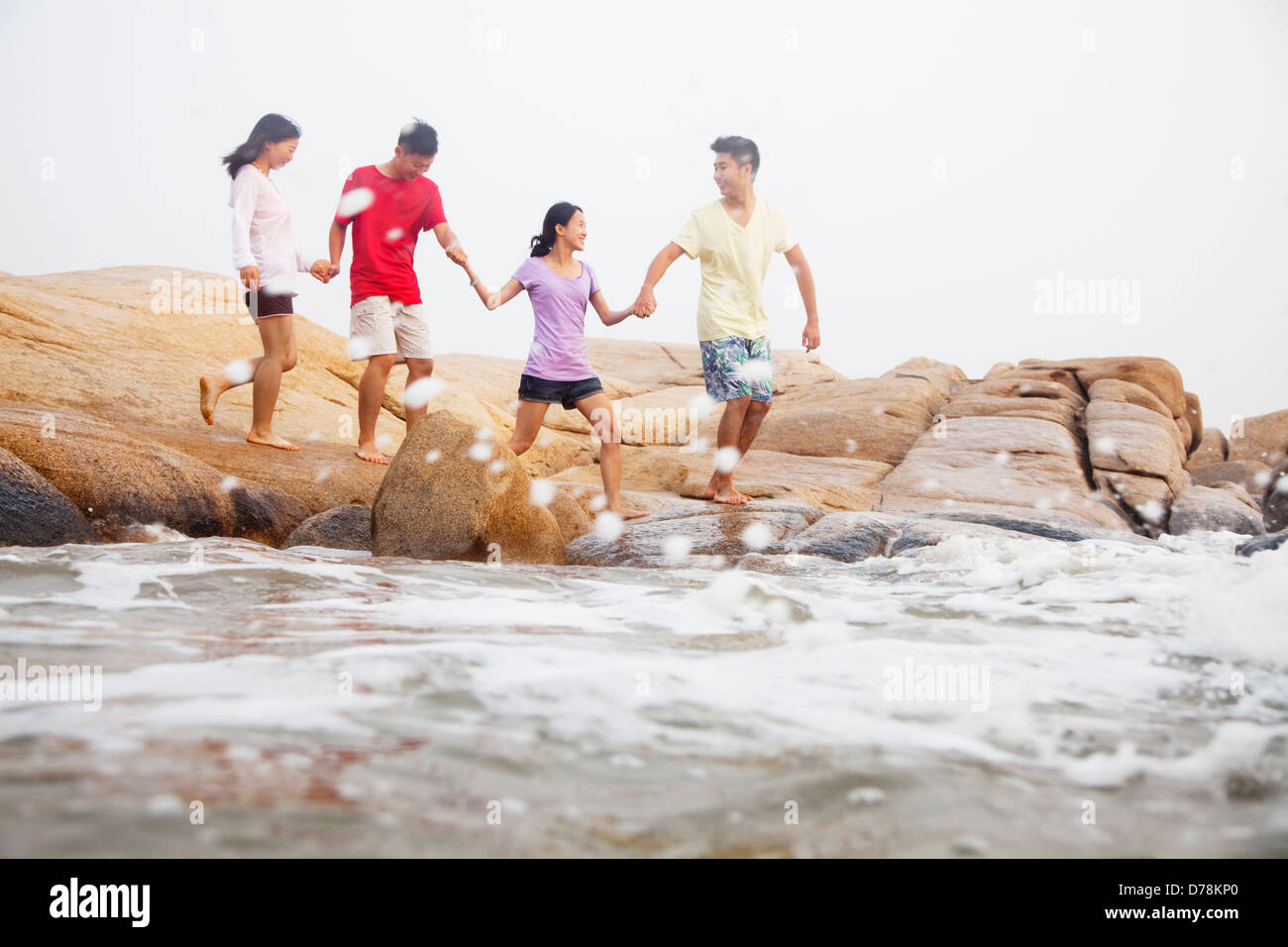 Four friends walking over rocks by the sea Stock Photo - Alamy