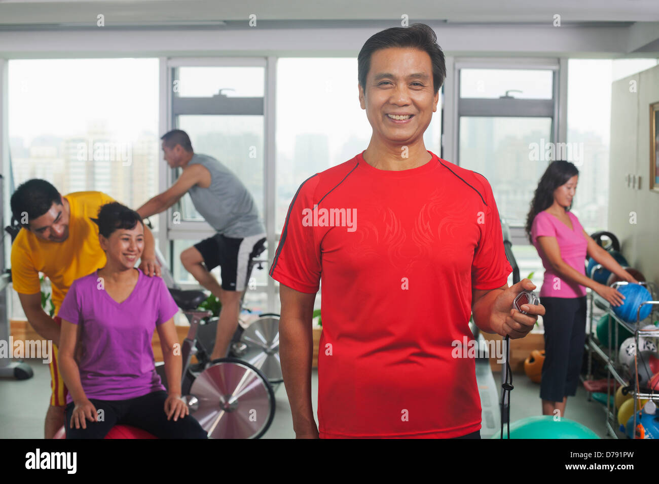 Man with stopwatch on the foreground, people working out in the gym on ...