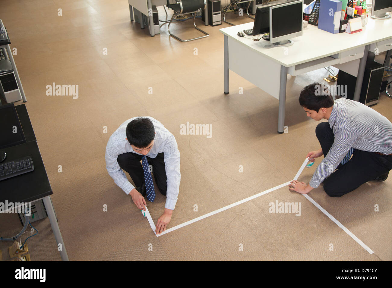Two young businessmen taping up the floor in the office Stock Photo - Alamy