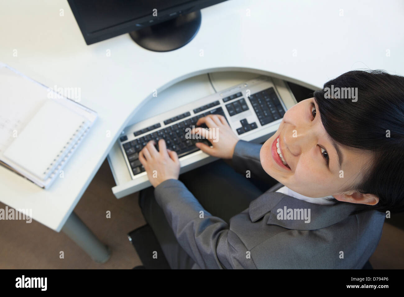 Young businesswoman sitting at desk, looking up smiling Stock Photo - Alamy