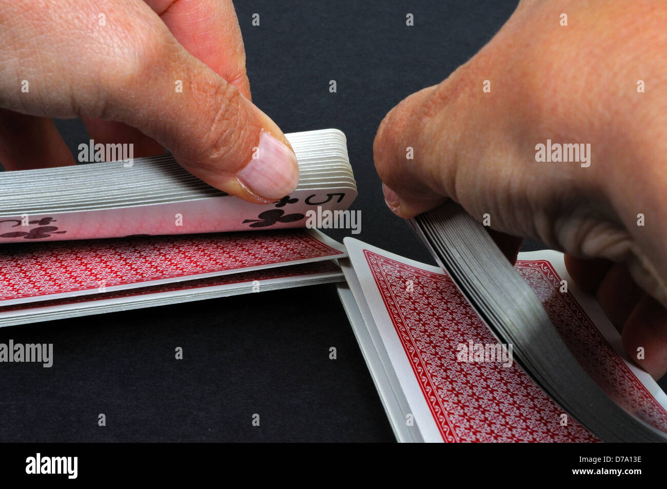 Woman shuffling a pack of playing cards against a plain black ...