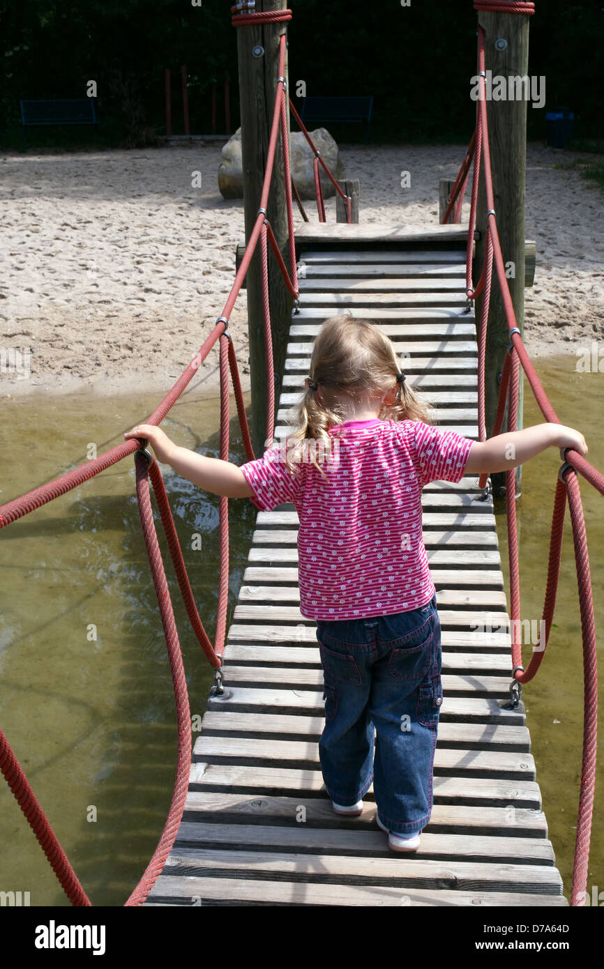 little girl walking on a suspended wooden bridge back view Stock Photo ...