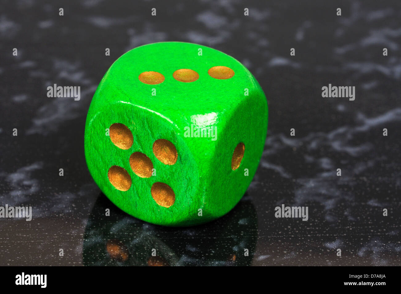 Platonic regular 6 sided green die with gold pips against a black and ...