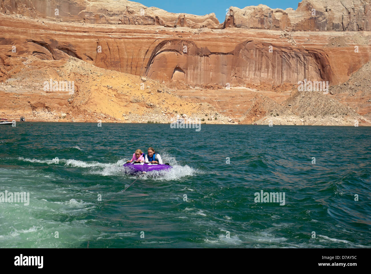 Mother and daughter ride on purple towable tube behind speedboat on ...