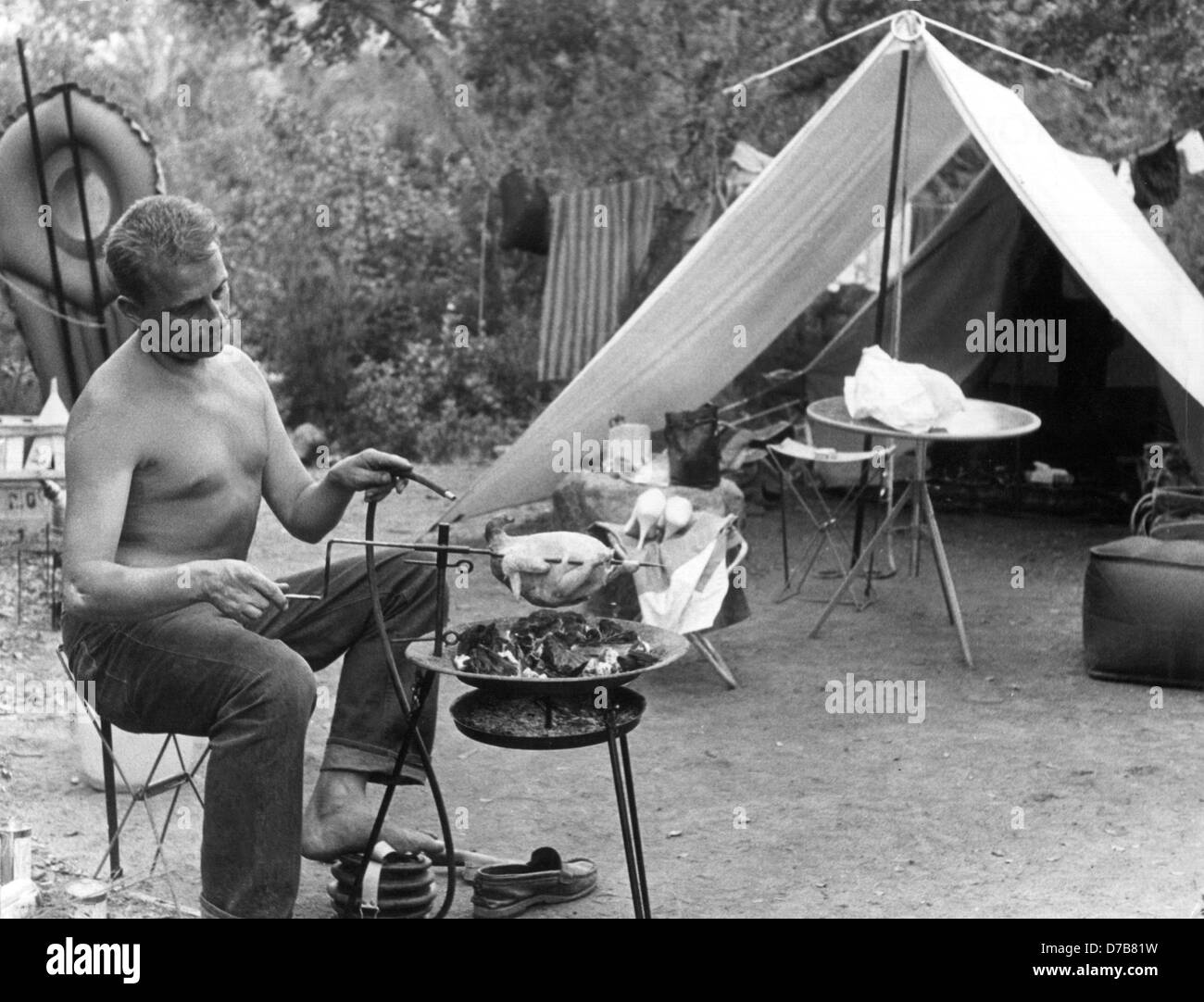 A camper grills a roast chicken in front of his tent in July 1957 Stock ...