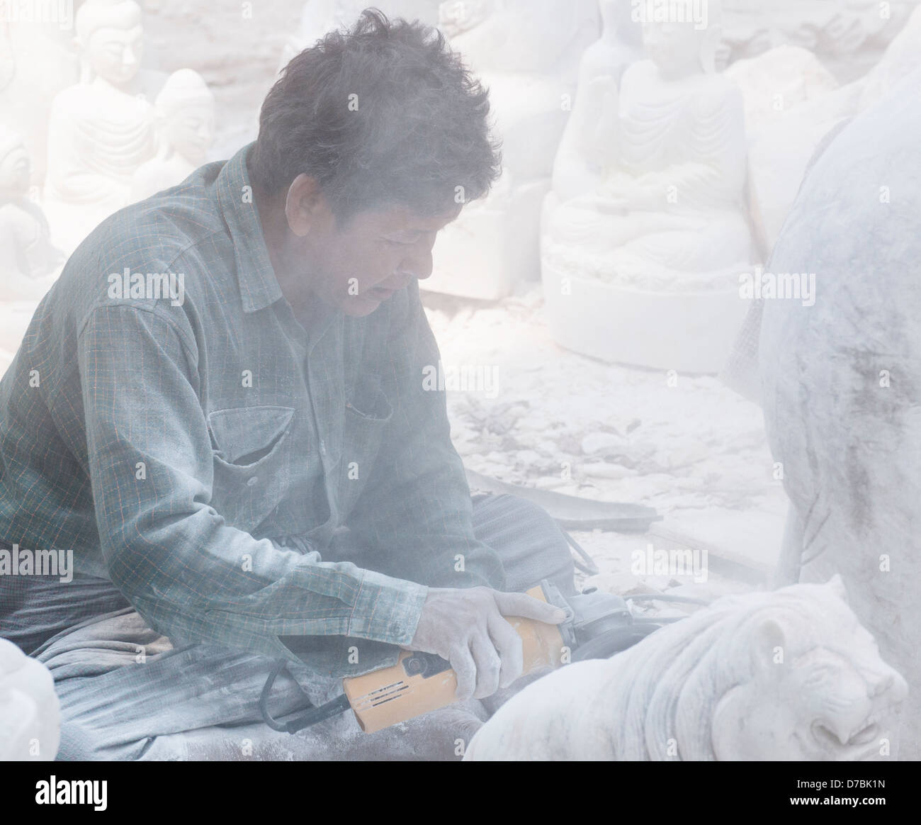 A craftsman chisels marble into a Buddha statue at a stone workshop ...
