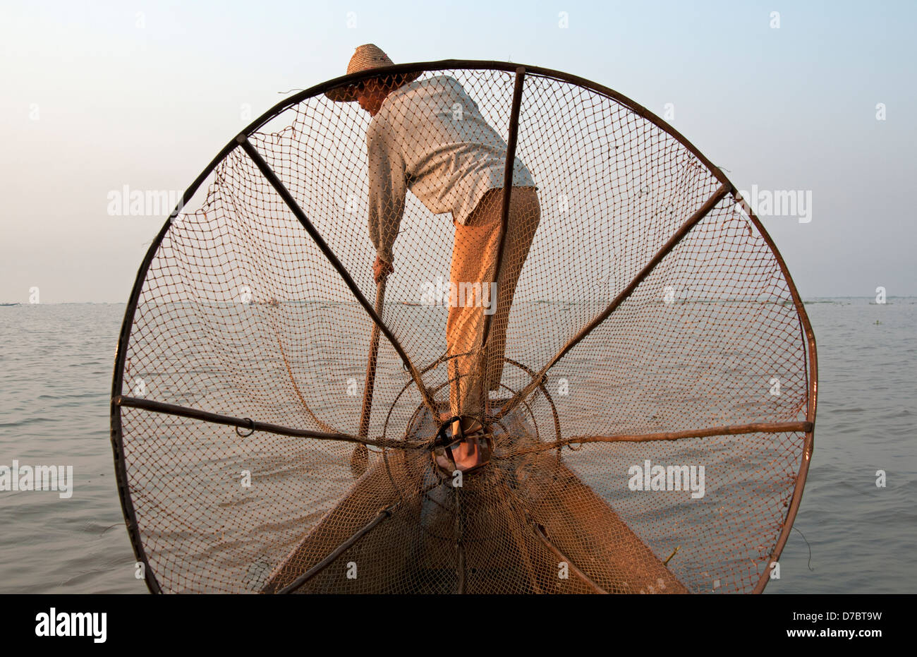 Intha leg rowing fisherman seen through his cone shaped net on Inle ...