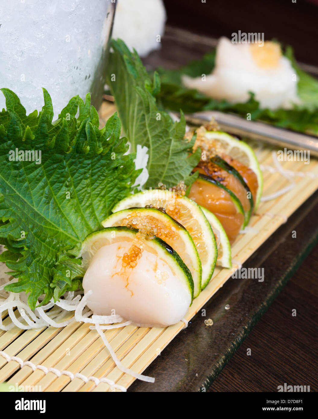 Detail of sashimi display in restaurant, scallops and lime on bamboo ...