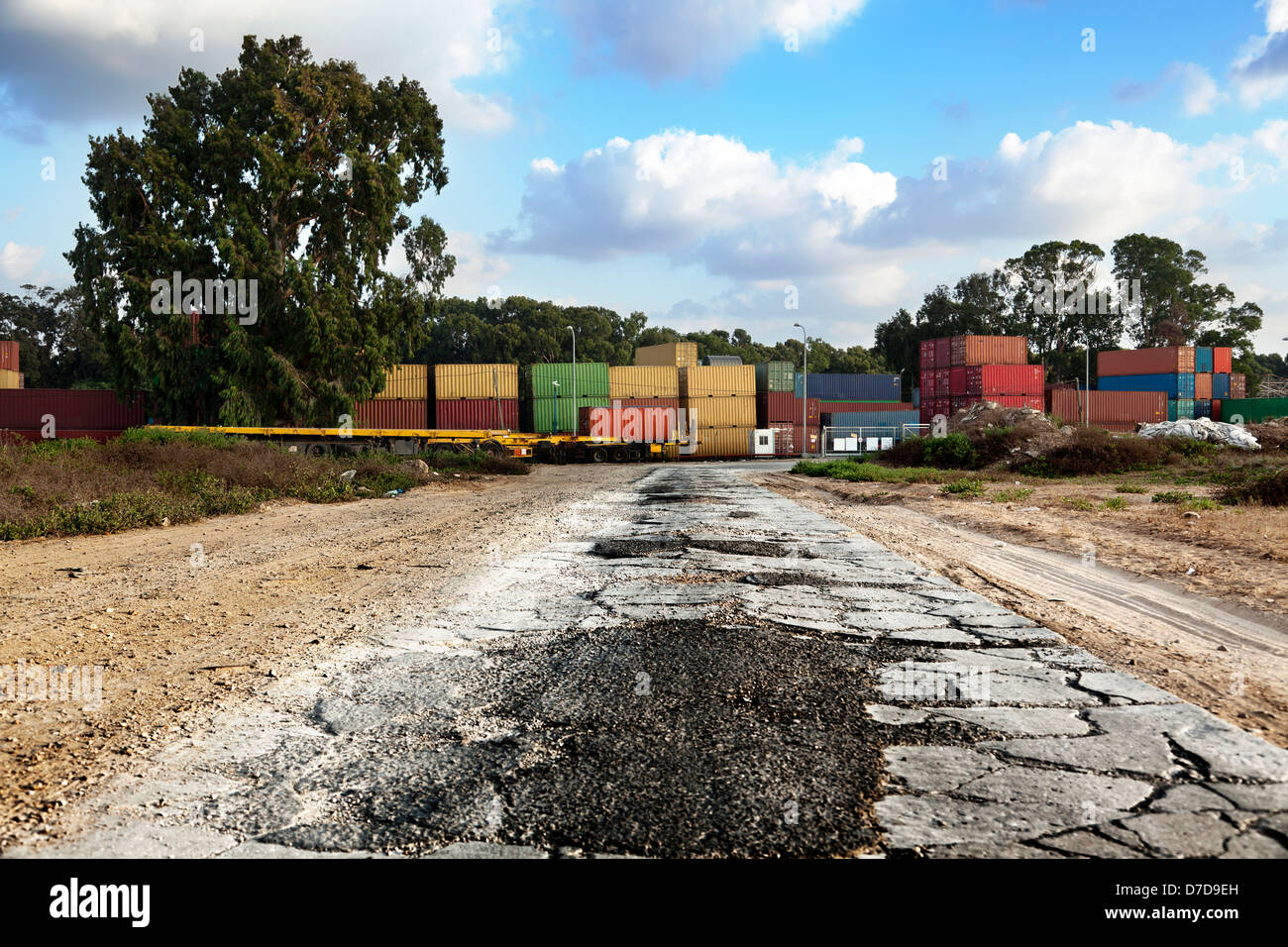 A badly patched broken asphalt road leads to a storage yard of cargo ...
