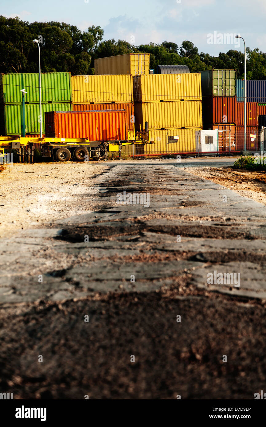 A badly patched broken asphalt road leads to a storage yard of cargo ...