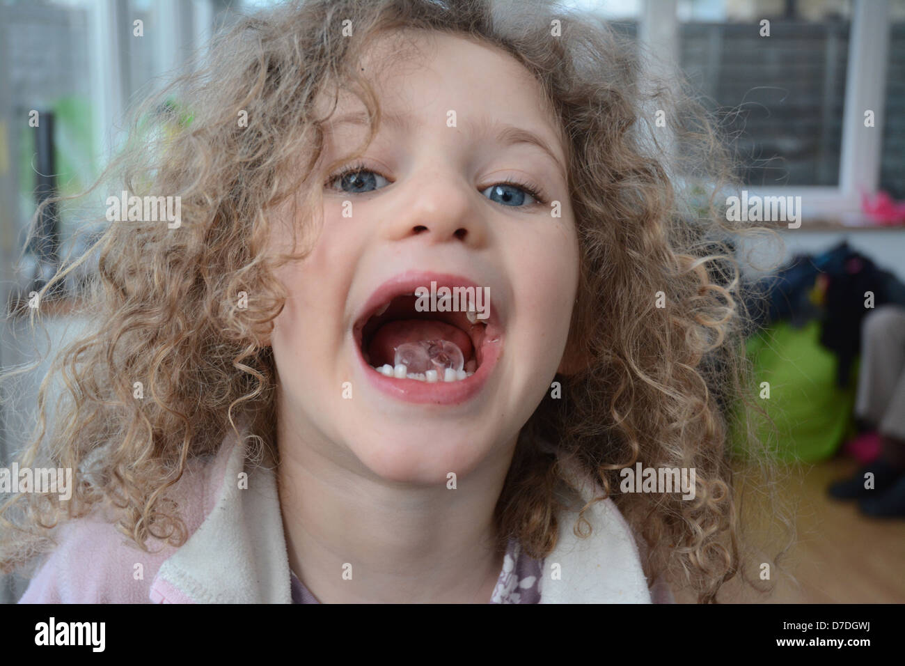 Five year old girl with curly hair and blue eyes showing an ice cube in ...