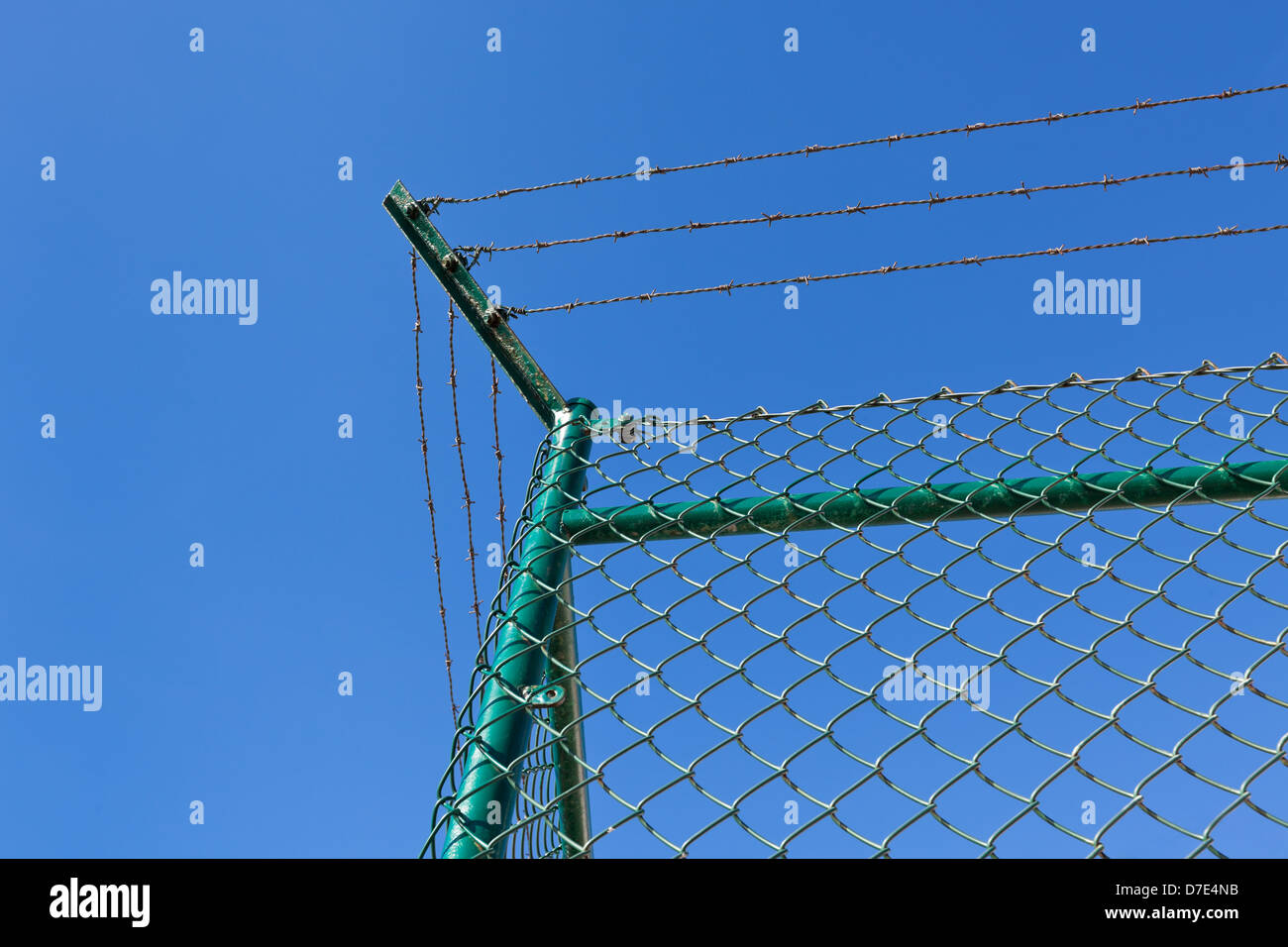 A chain link fence, topped by razor wire at bright blue sky background ...
