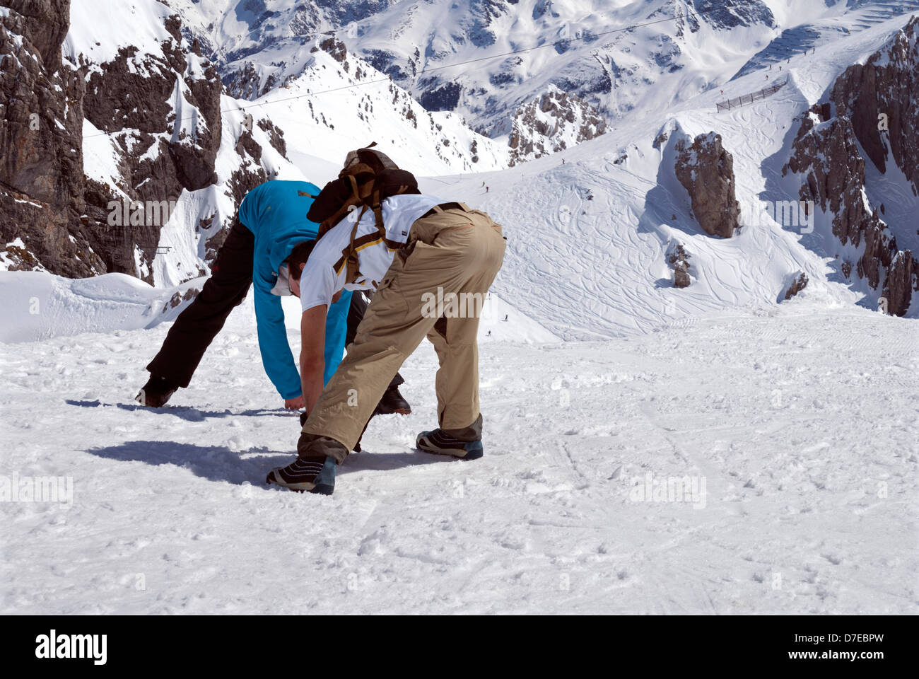 Two men performing pre-skiing warm-up stretching exercises, at altitude ...