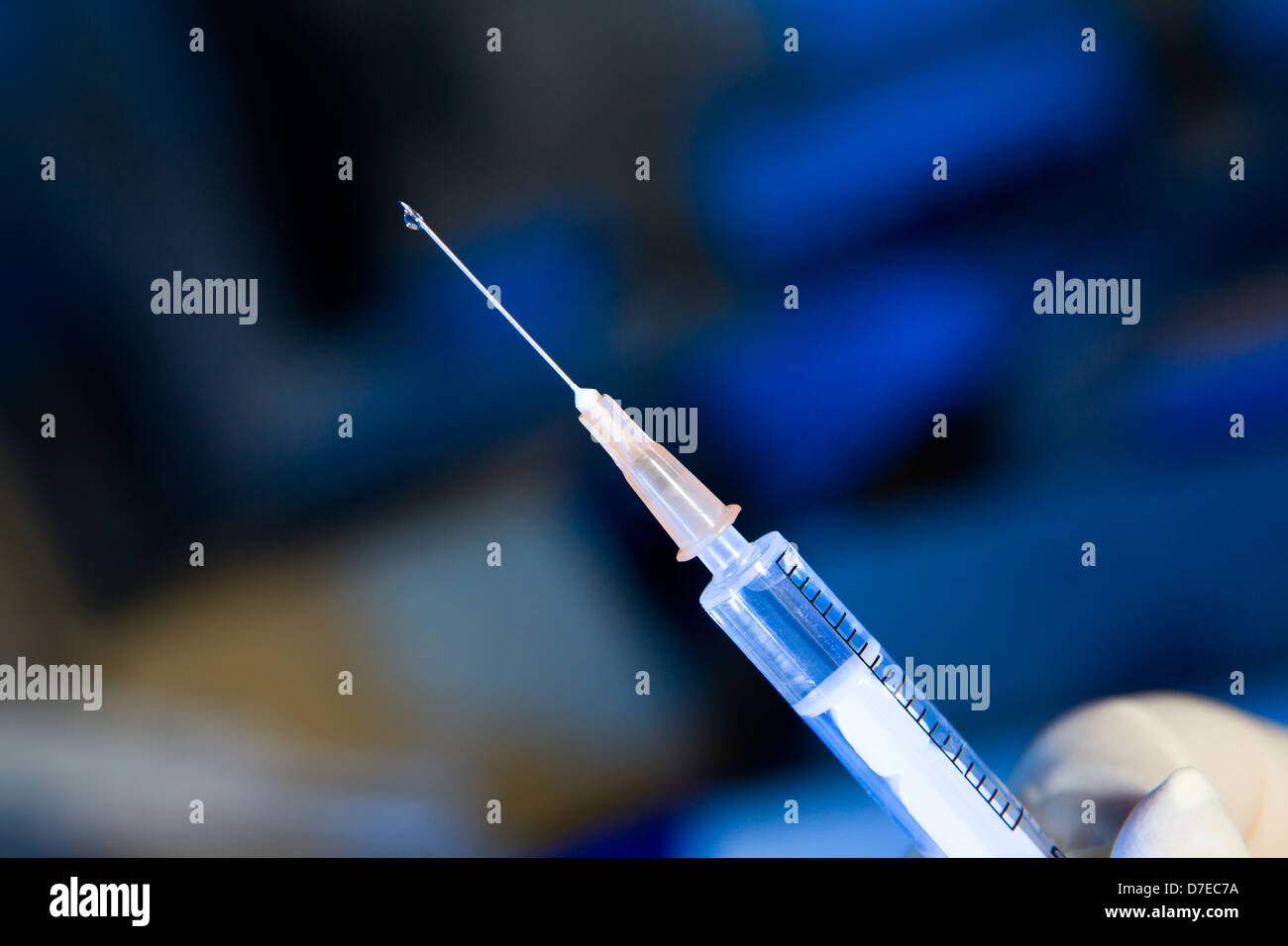 Syringe ready for injection with a drop of liquid, blue background ...