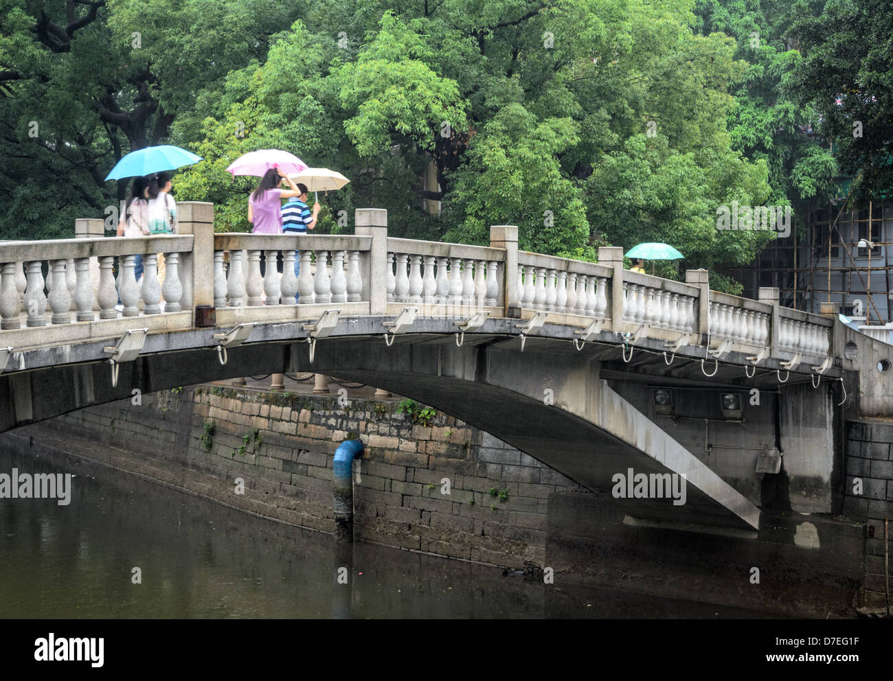 Traditional old arched Chinese bridge over a river with people crossing ...