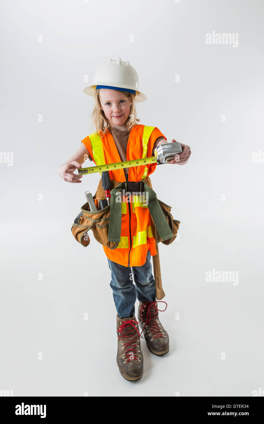 Young girl wearing oversized construction clothes and hard hat holding ...