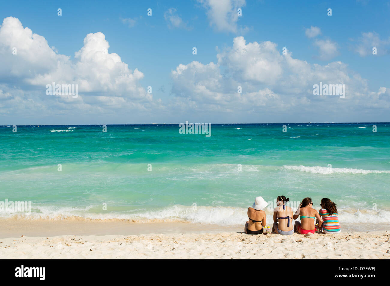 four young women in conversation on a beach sitting and facing the sea ...