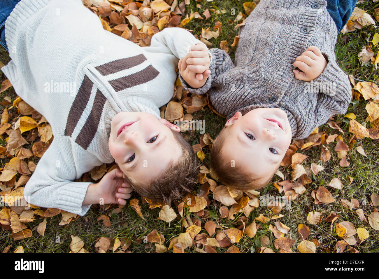 Portrait of two young boys laying on the ground in fallen autumn leaves ...
