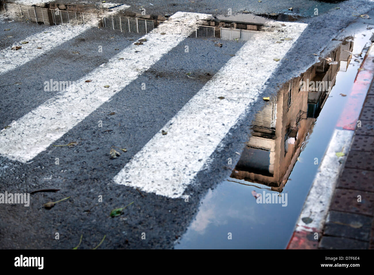A Tel-Aviv building reflecting in a puddle that's between the curb and ...