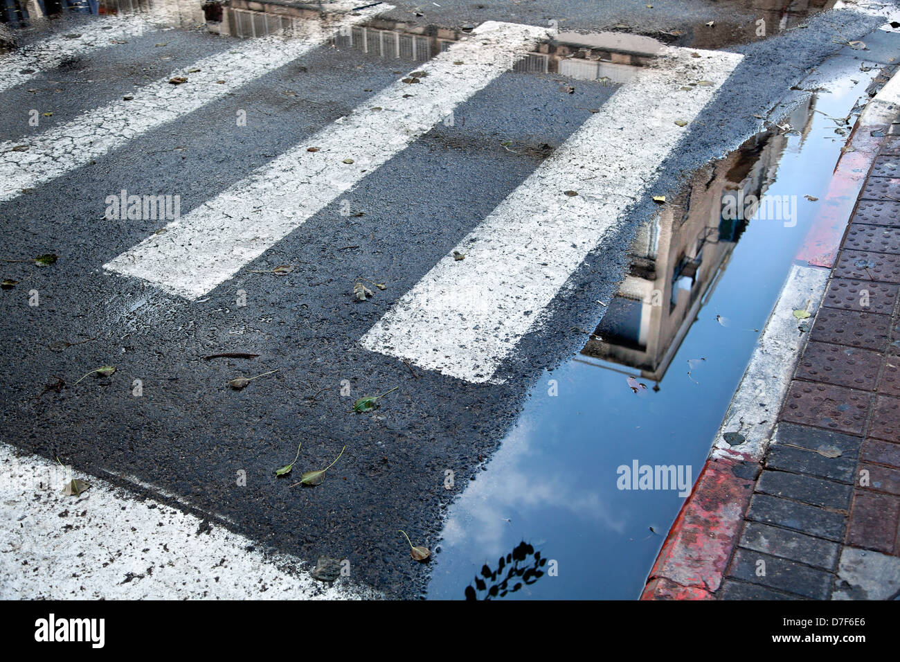 A Tel-Aviv building reflecting in a puddle that's between the curb and ...