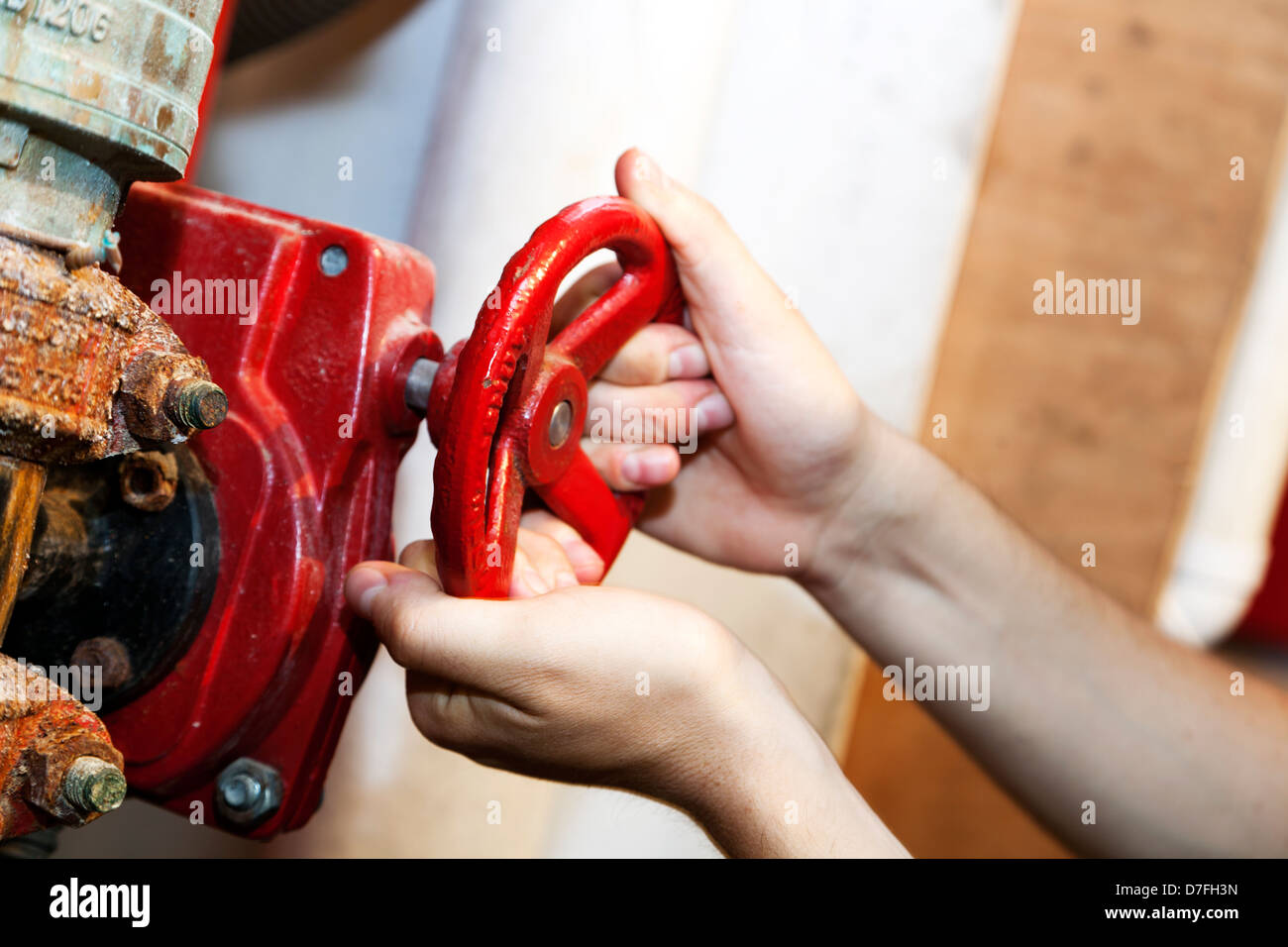 The hands of an adult man in the action of turning a bright red valve ...