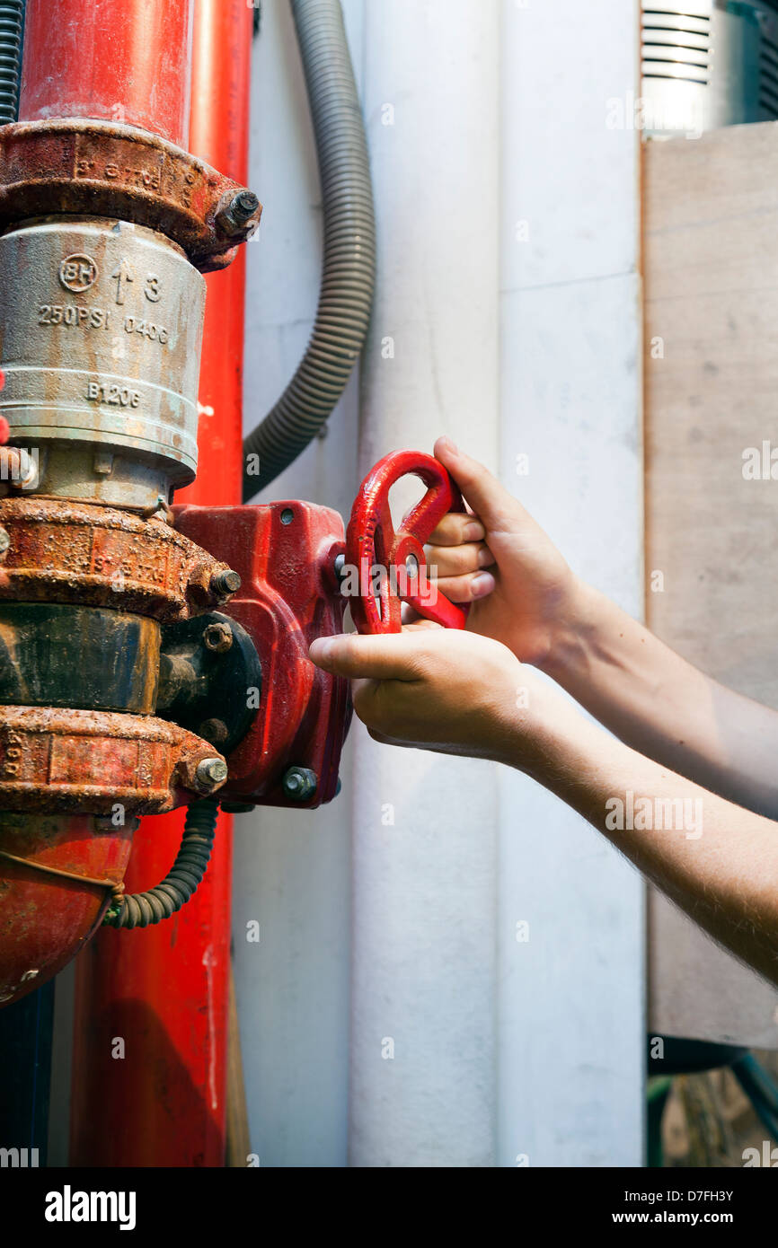 The hands of an adult man in the action of turning a bright red valve ...