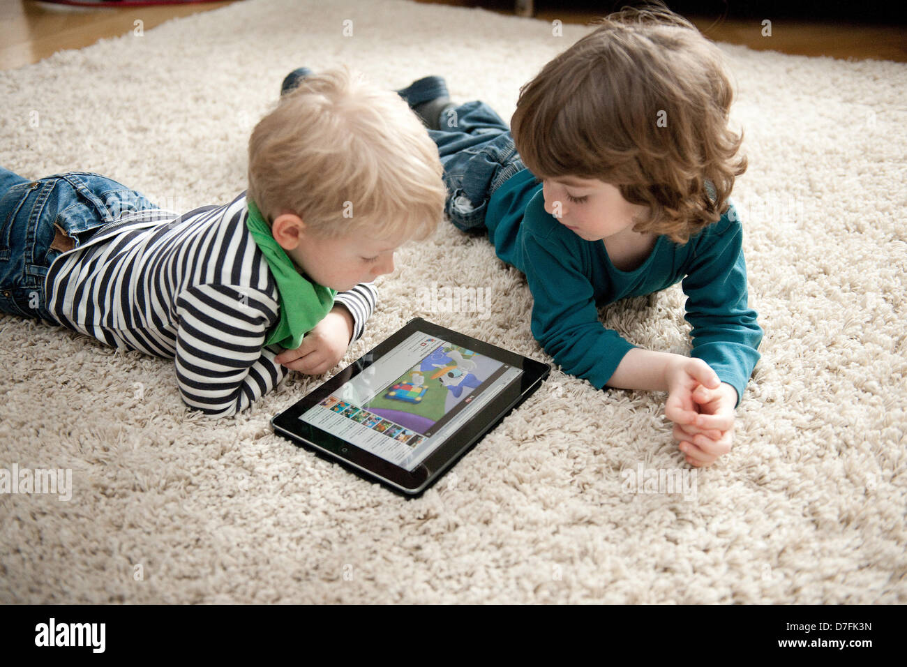 Two little boys are lying on the floor watching an animated cartoon on ...