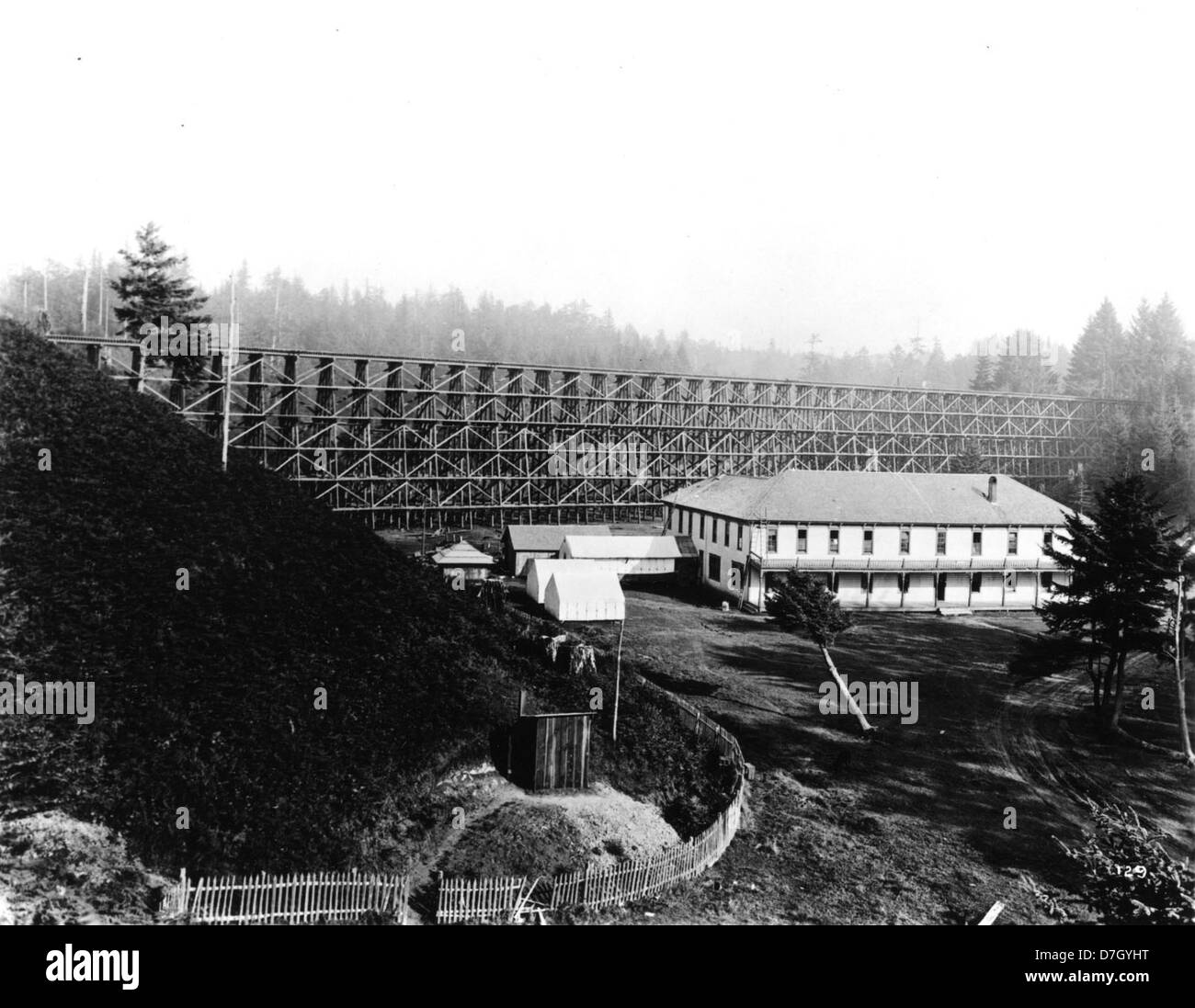 This image shows a spruce camp near a railroad trestle, located near ...