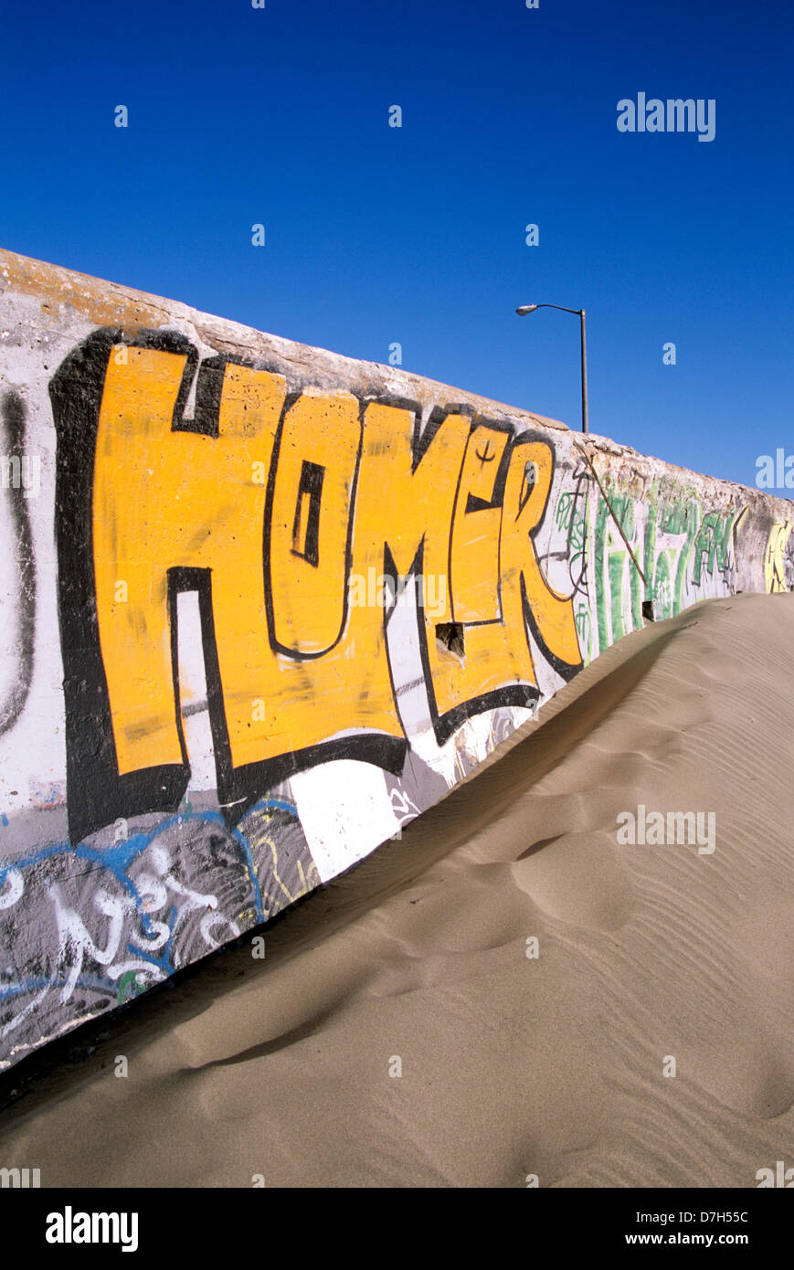 view of graffiti painted sea wall being covered with wind blown sand ...