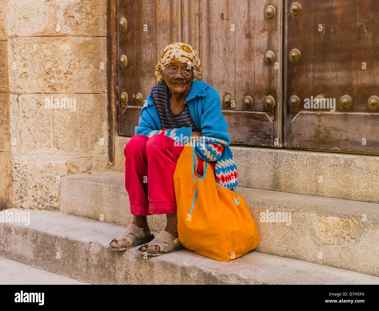 An elderly black woman sits on a stone stoop in Havana, Cuba with an ...