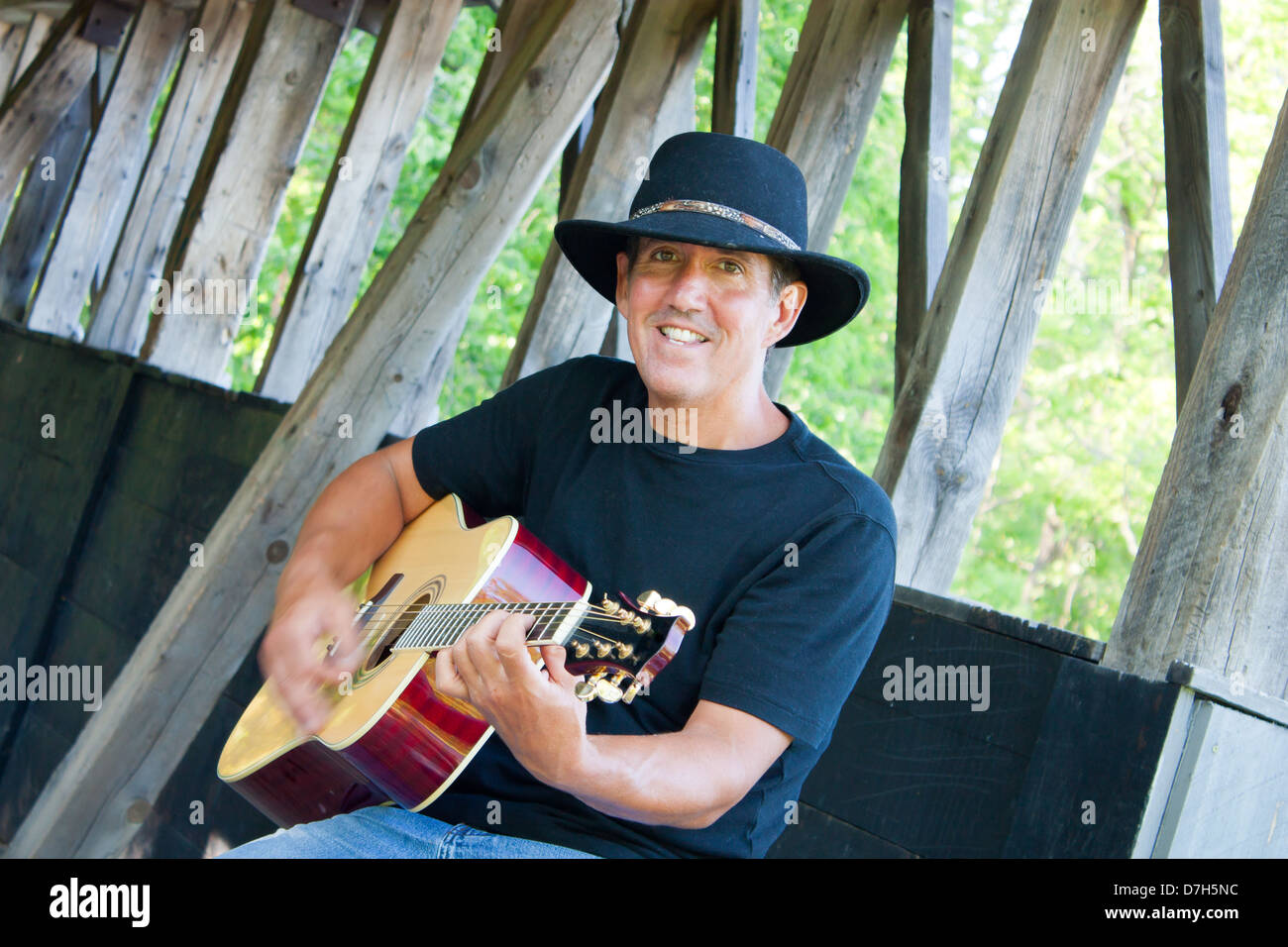 A man in jeans and cowboy hat plays guitar at the covered bridge Stock ...