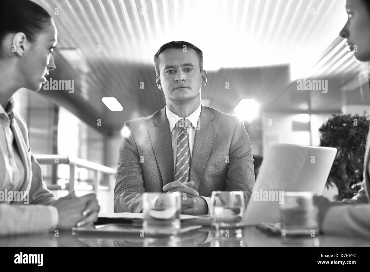 Serious boss looking at camera with his two employees sitting near by ...