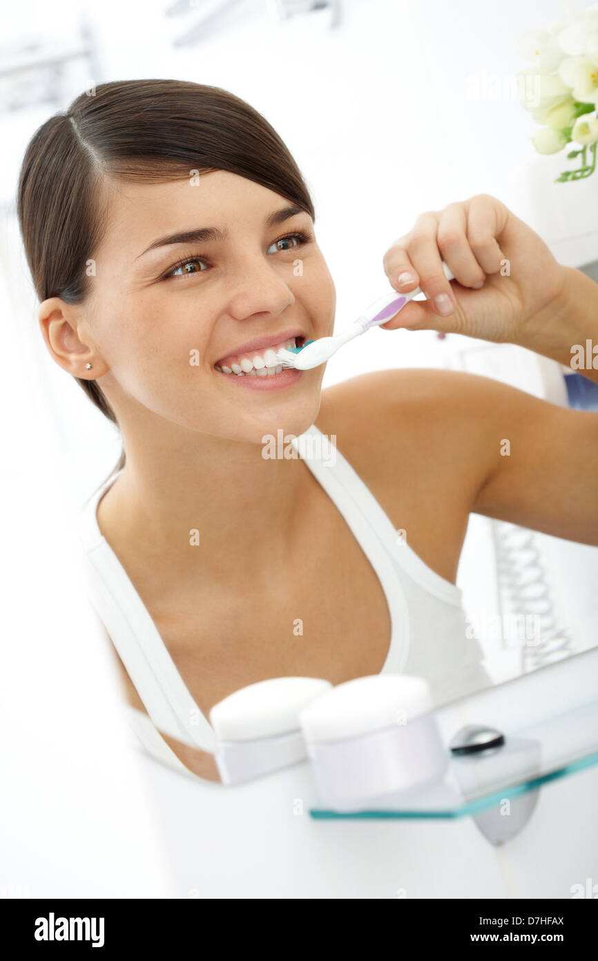 Image Of Pretty Female Brushing Her Teeth In Front Of Mirror In The