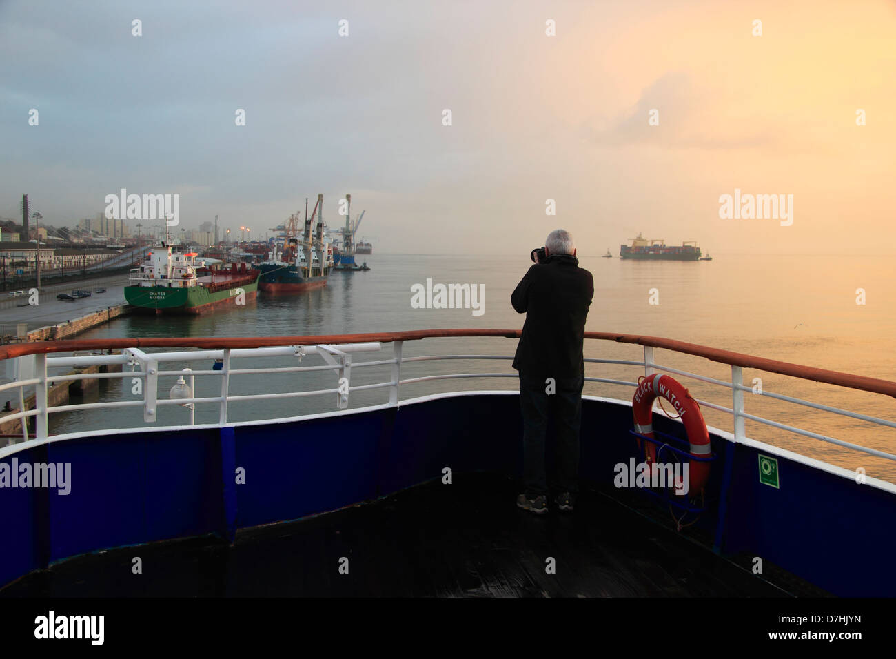 Man taking a photograph of the docks at dawn, from the deck of a cruise ...