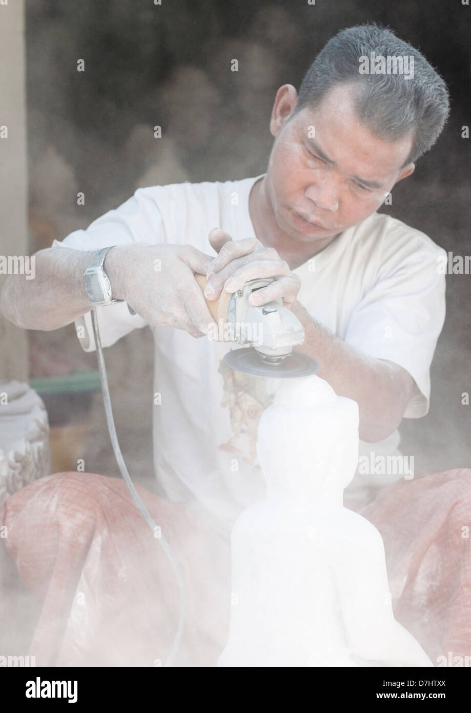 A craftsman chisels marble into a Buddha statue at a stone workshop ...