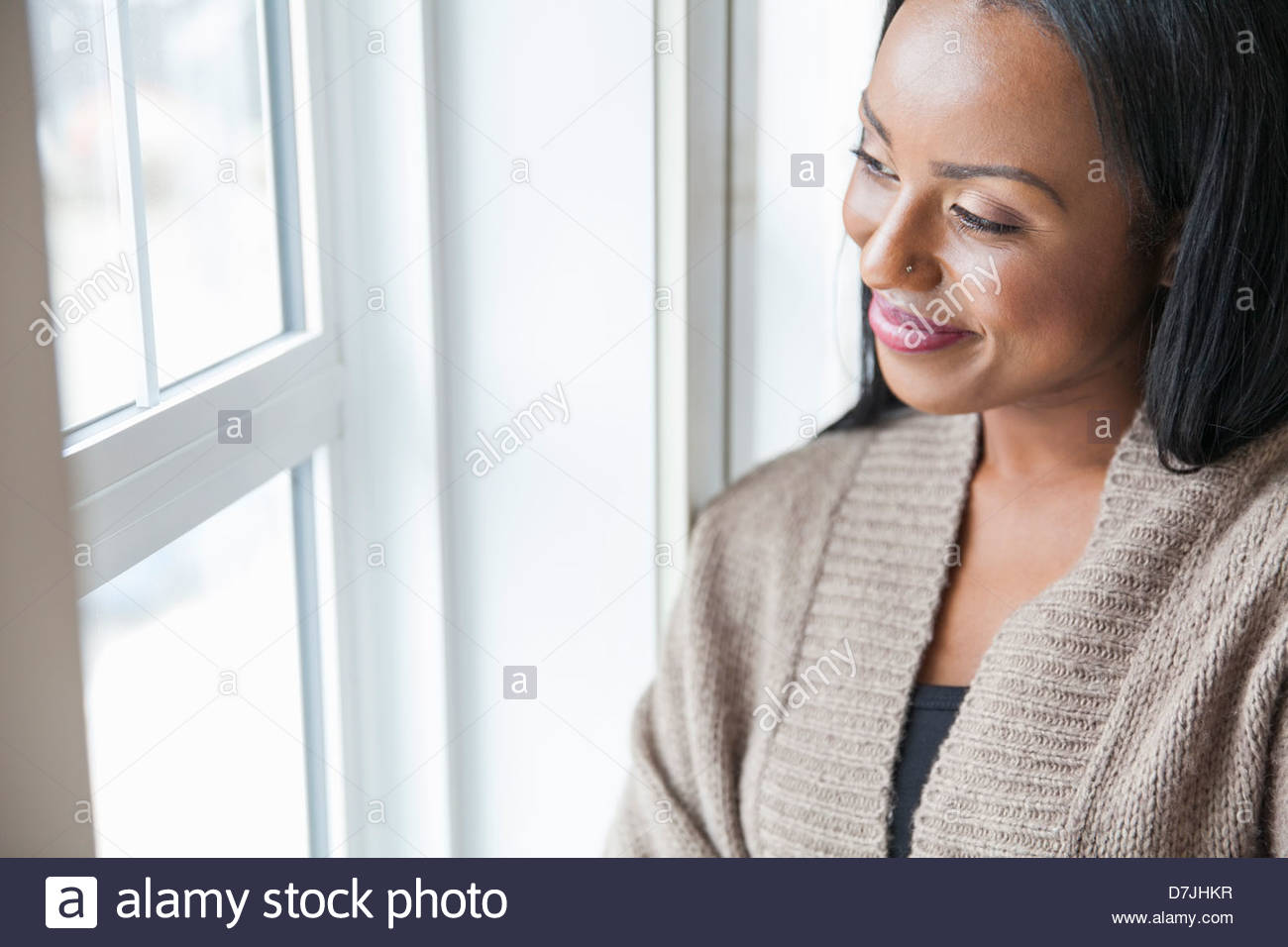Smiling woman looking out window at home Stock Photo - Alamy