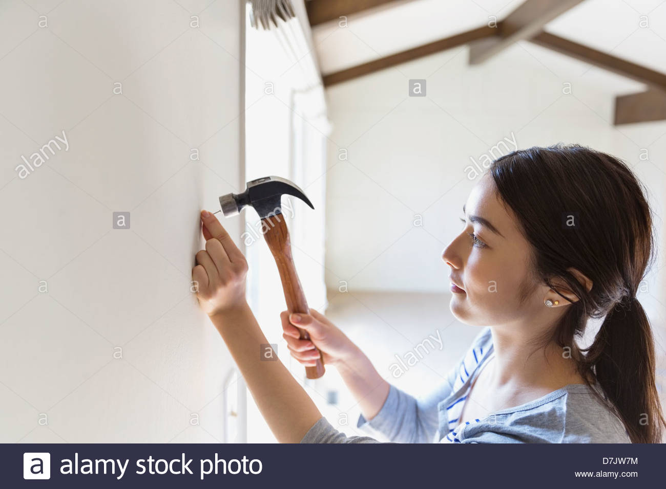 Young woman hammering nail into wall at home Stock Photo - Alamy