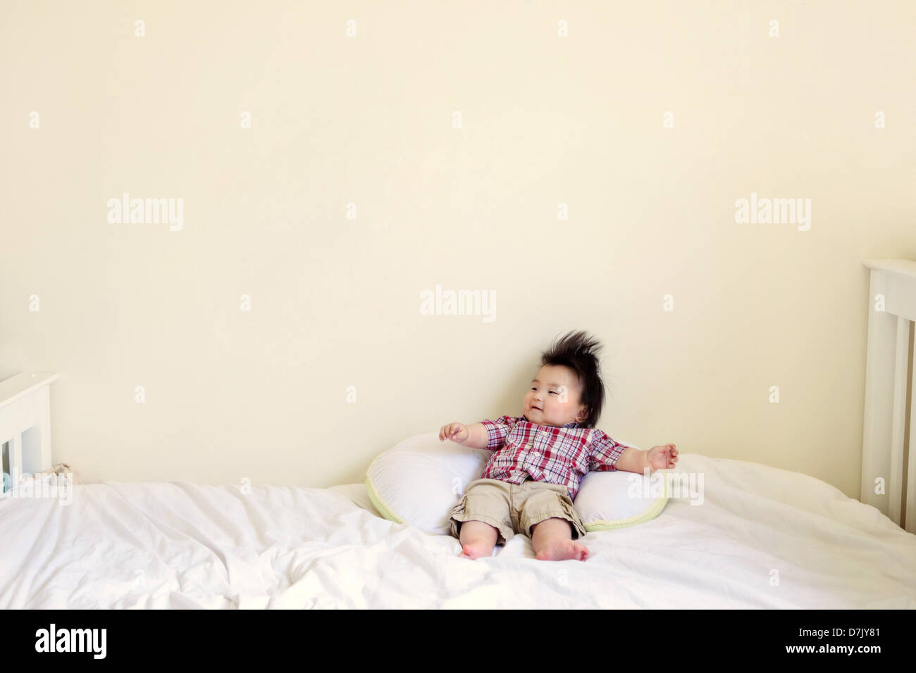 Korean American child with spiky black hair relaxing on bed arms ...
