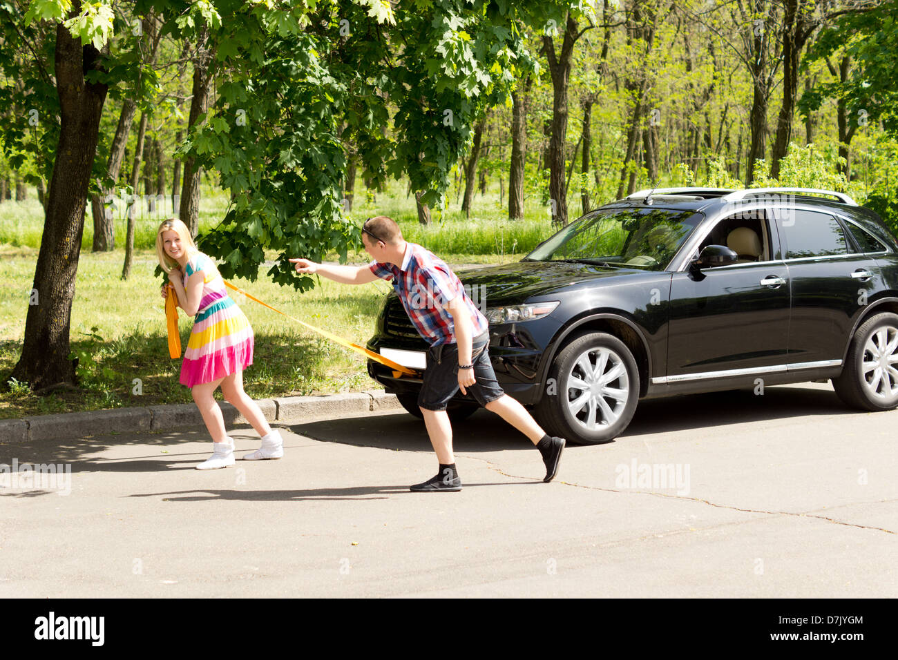 Lazy man watching his girlfriend pull a car along by a strap following ...
