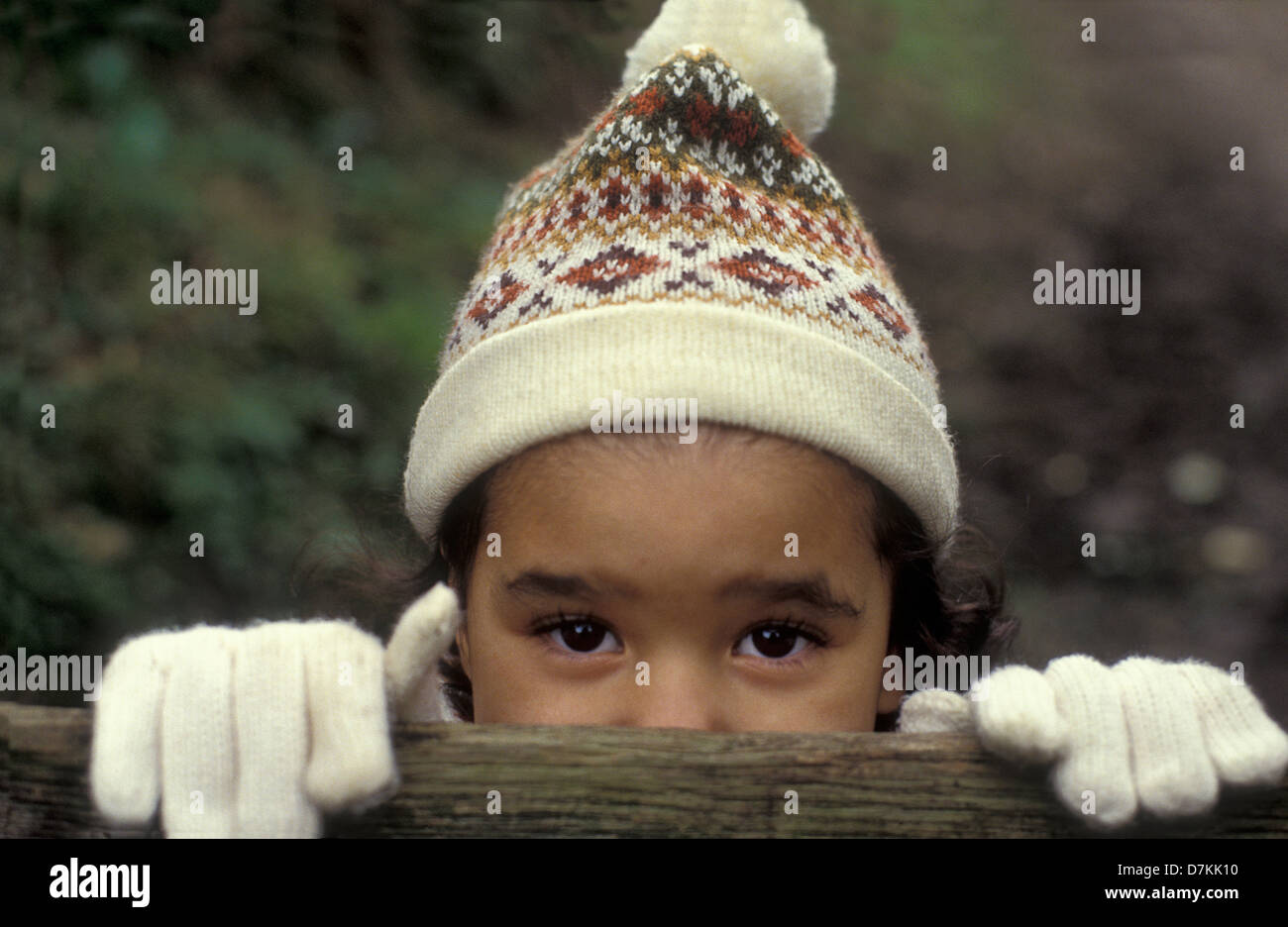 little girl in bobble hat peering over fence Stock Photo - Alamy