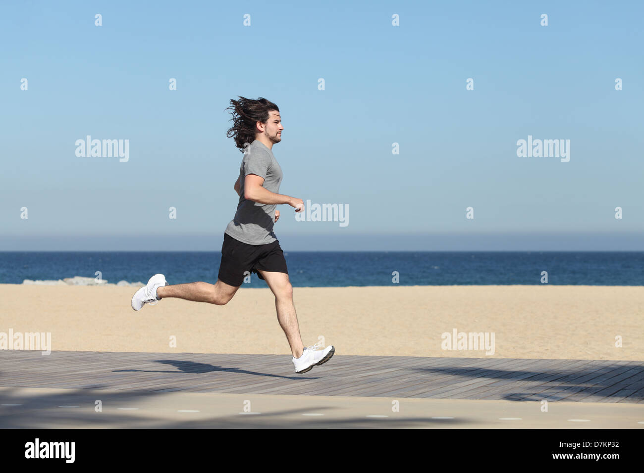 Side view of a man running on the seafront of the beach with the sea in ...